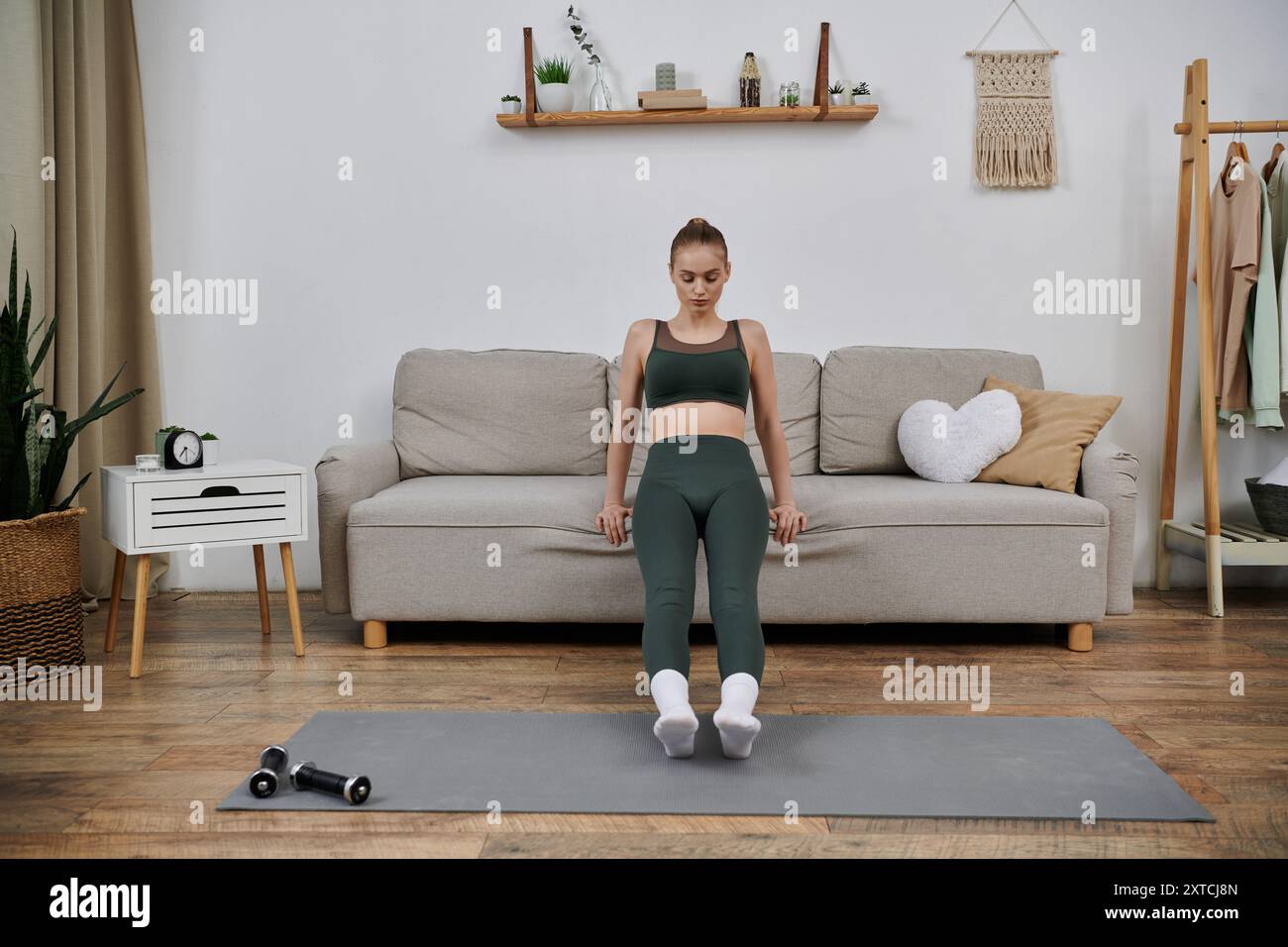 A young woman performs an exercise using a couch for support in her ...