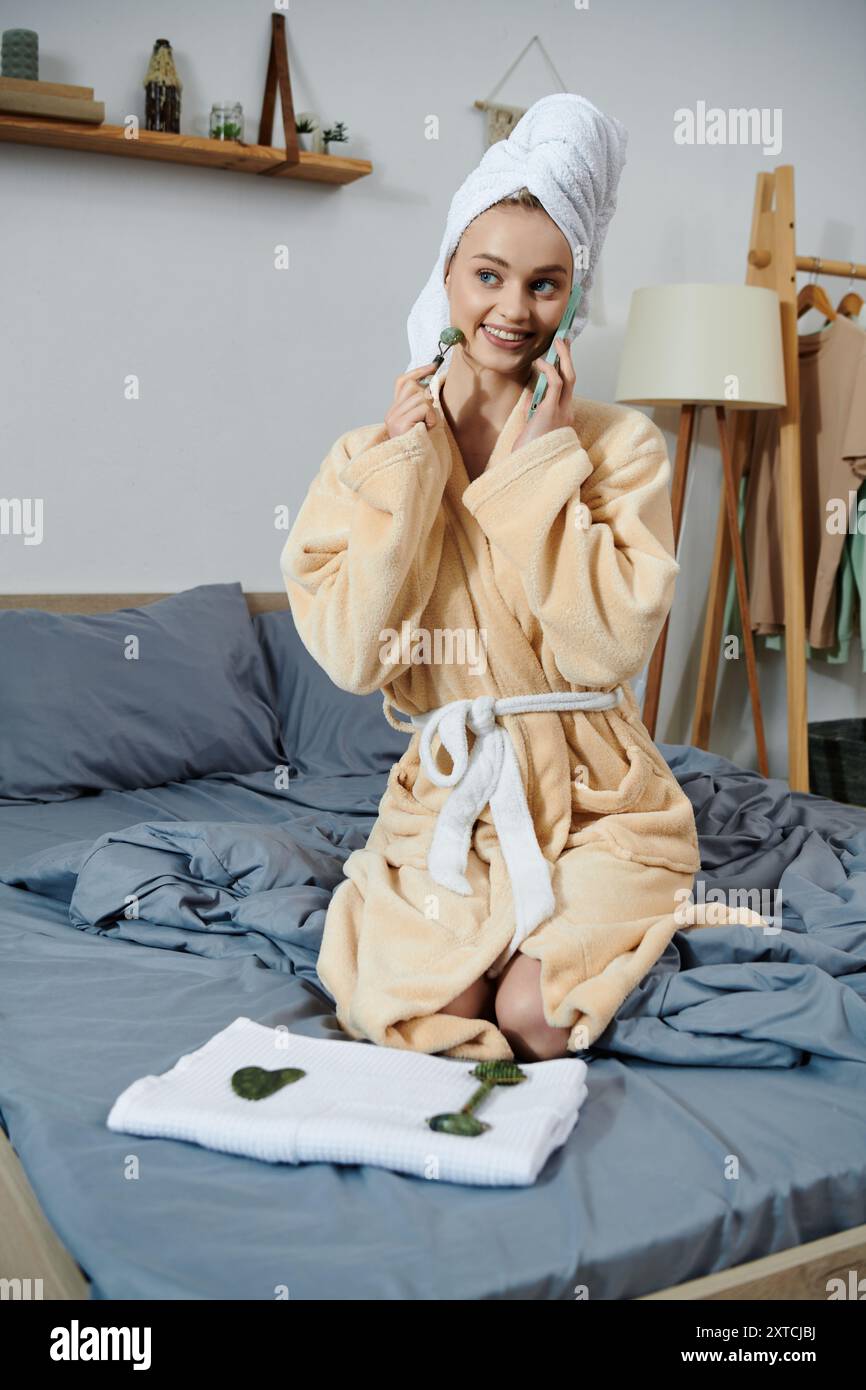 A young woman in a bathrobe and towel sits on a bed, enjoying her ...