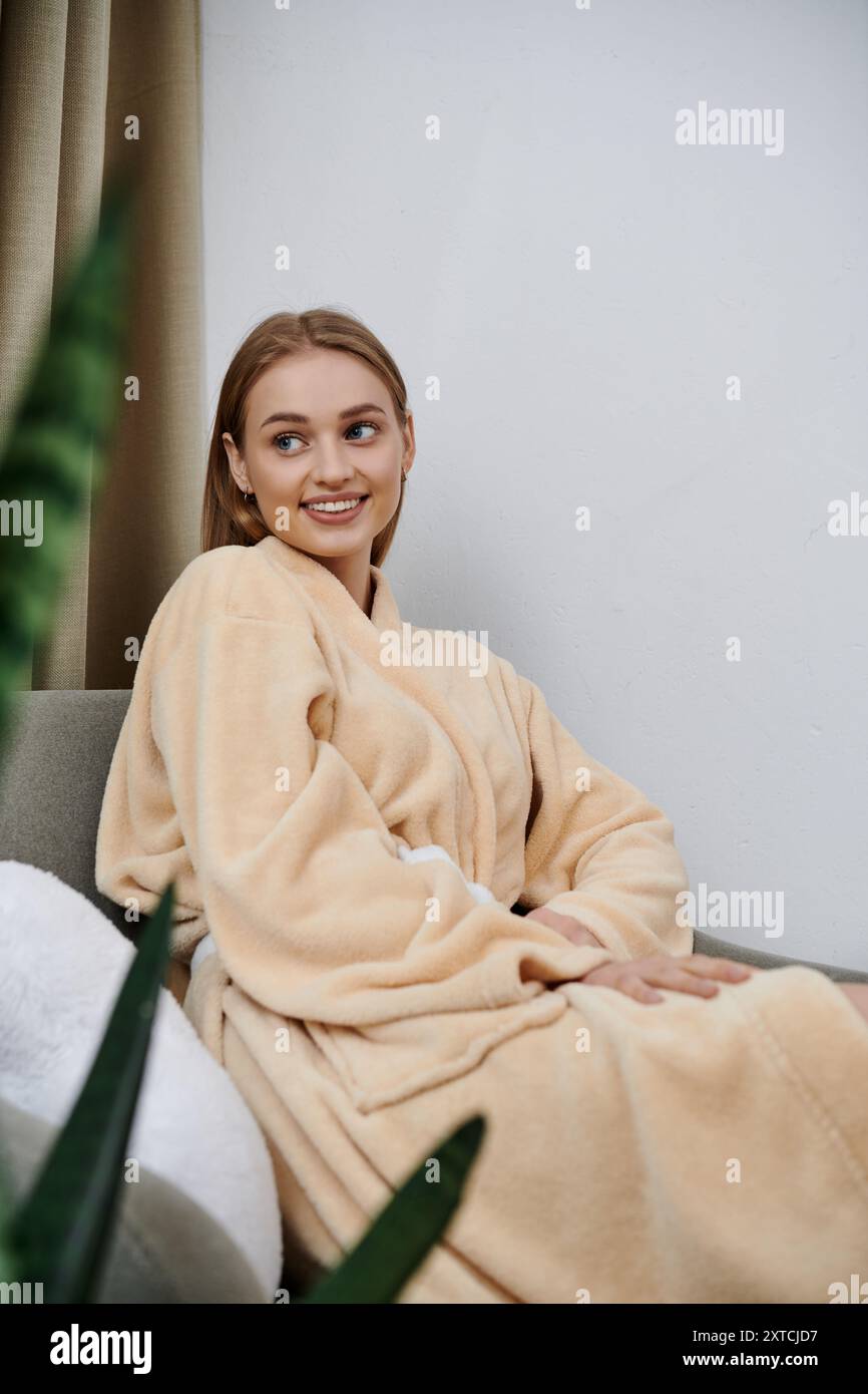 A young woman relaxes in a plush robe at home, enjoying a quiet moment ...