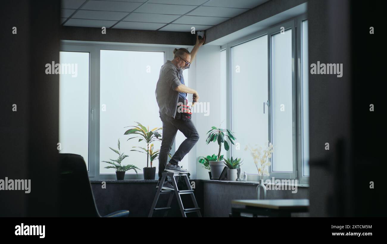 Professional male installer in uniform stands on ladder and screws ...