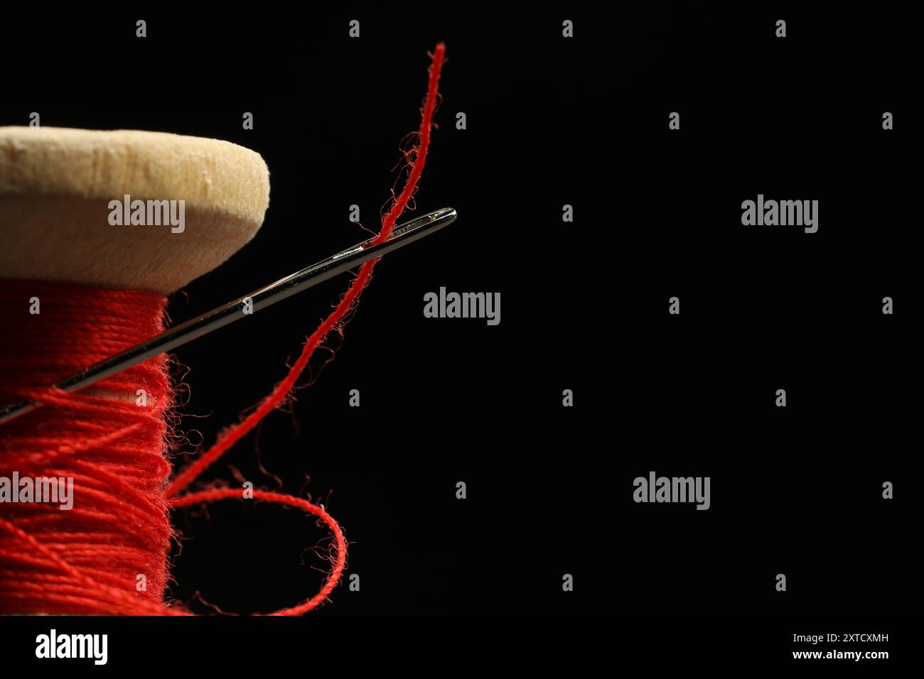 Spool of red sewing thread with needle on black background, closeup ...