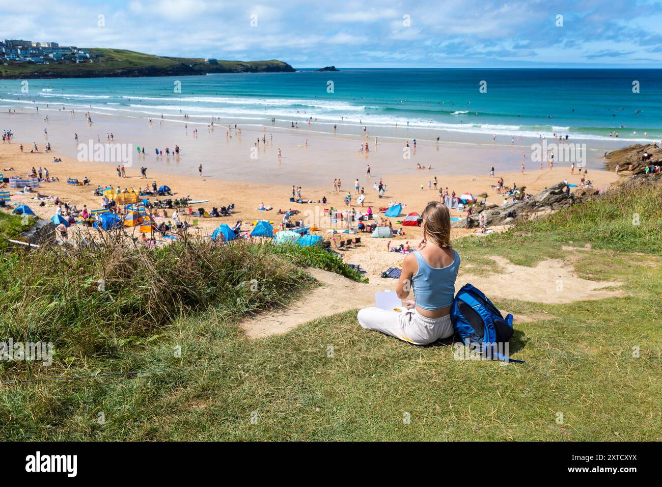 A young female holidaymaker sitting alone on the coast overlooking a ...