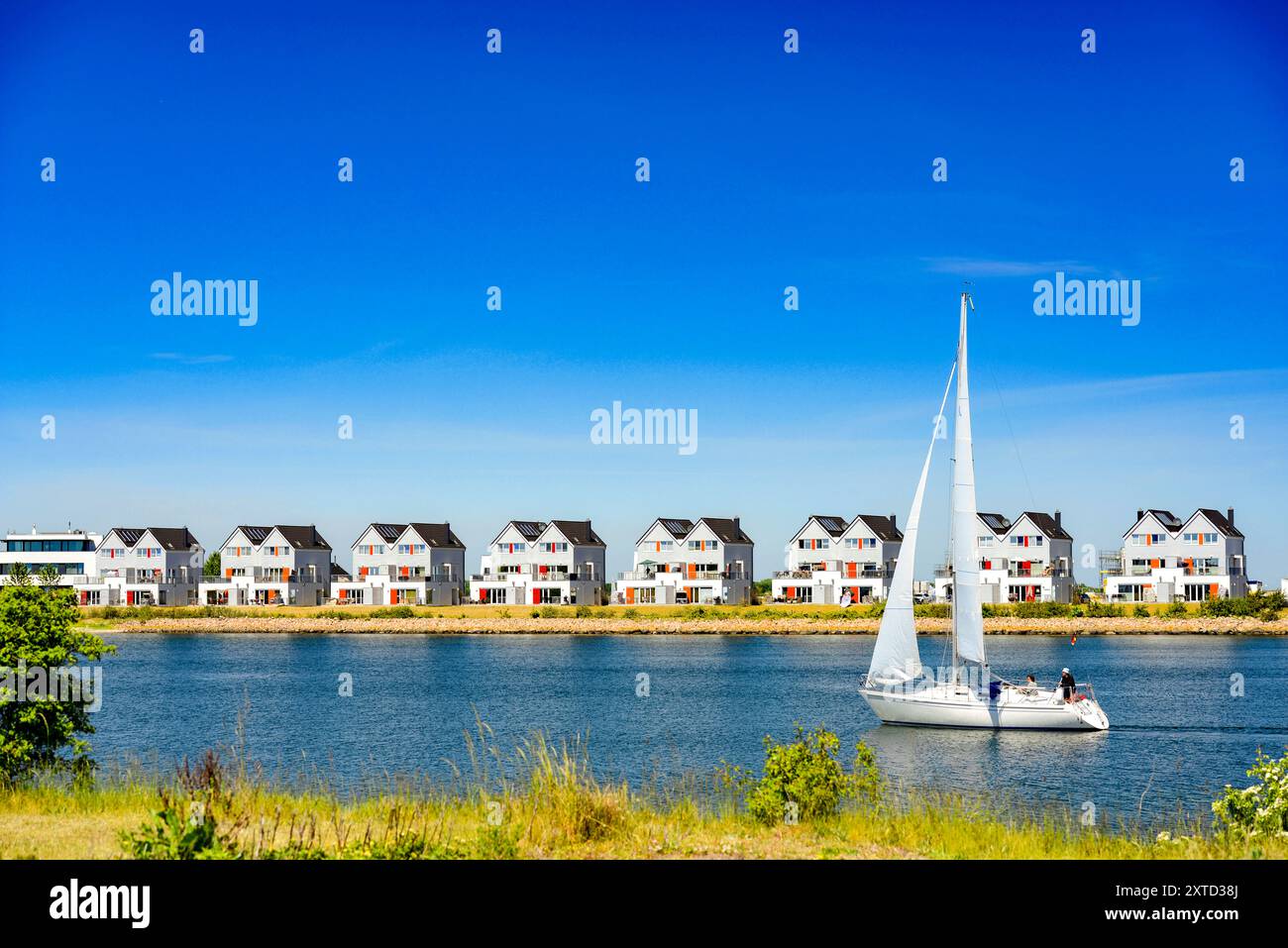 Cottages on a river bank with white sailing ship under a clear blue sky ...