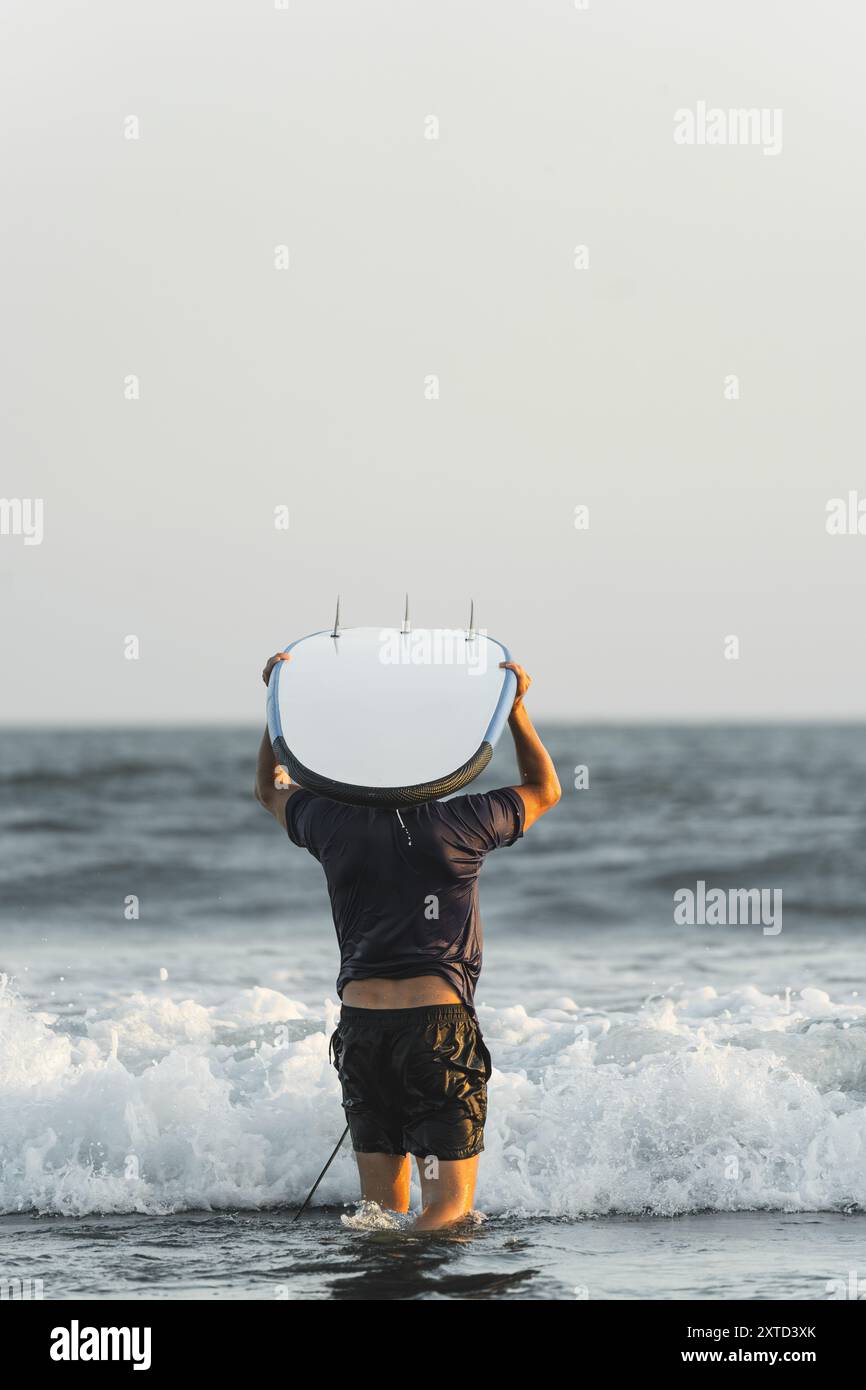 Unrecognizable surfer entering the ocean with his surfboard overhead ...