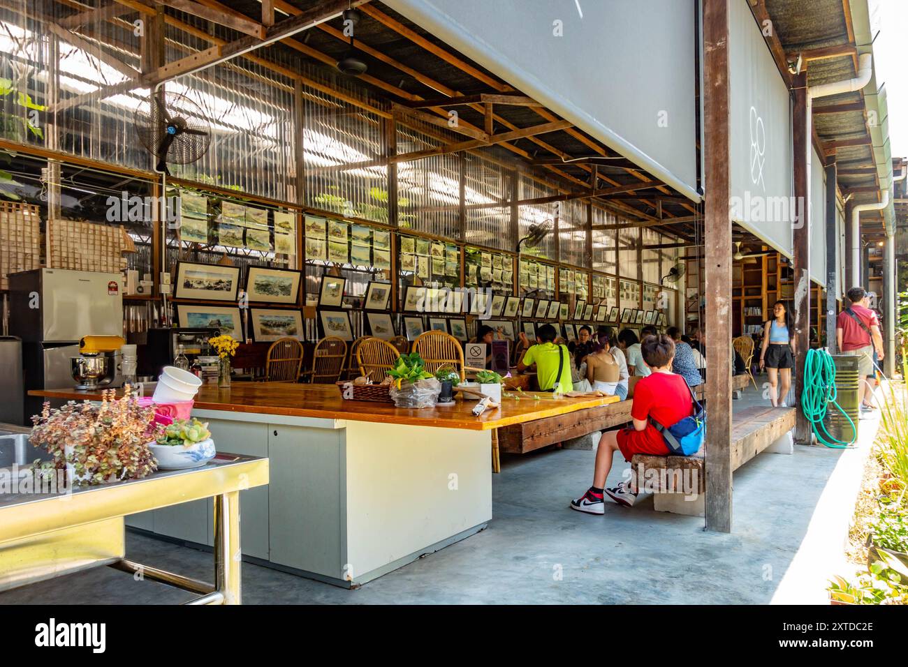 People sit and eat at a large wooden table. On one side, watercolour paintings are displayed for ...