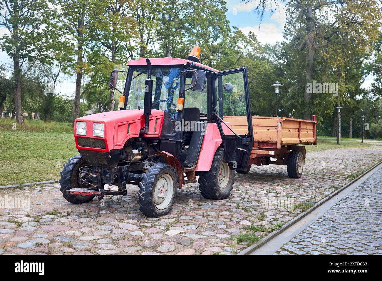 Small mini red tractor with trailer standing at stone farm road sunny ...