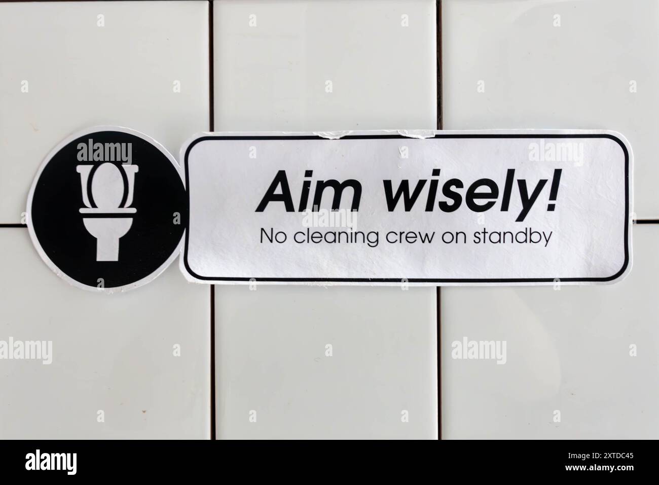 A humorous notice on a white tiled wall in a men's pubic toilets asking ...