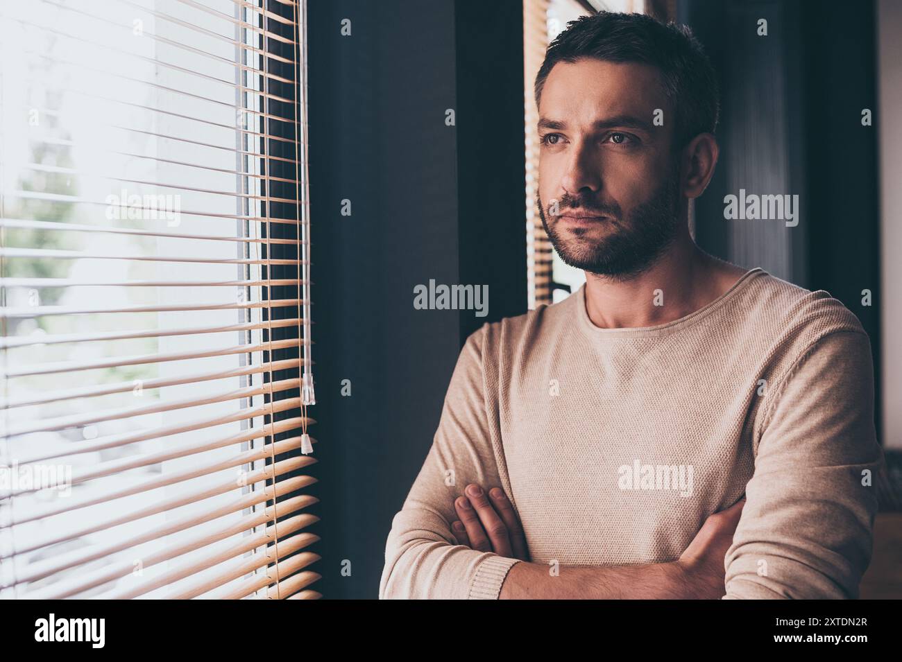 Handsome and thoughtful. Handsome young man looking trough window while ...