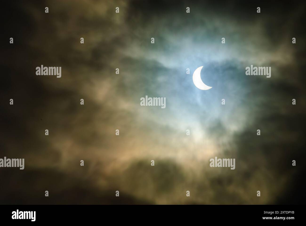 A crescent moon shines through dark, dramatic clouds amid a solar ...