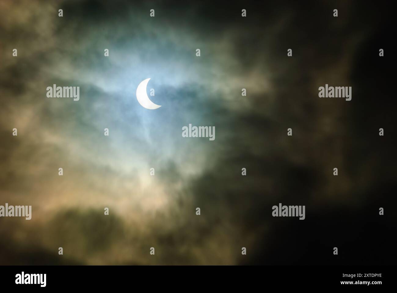 A crescent moon shines through dark, dramatic clouds amid a solar ...
