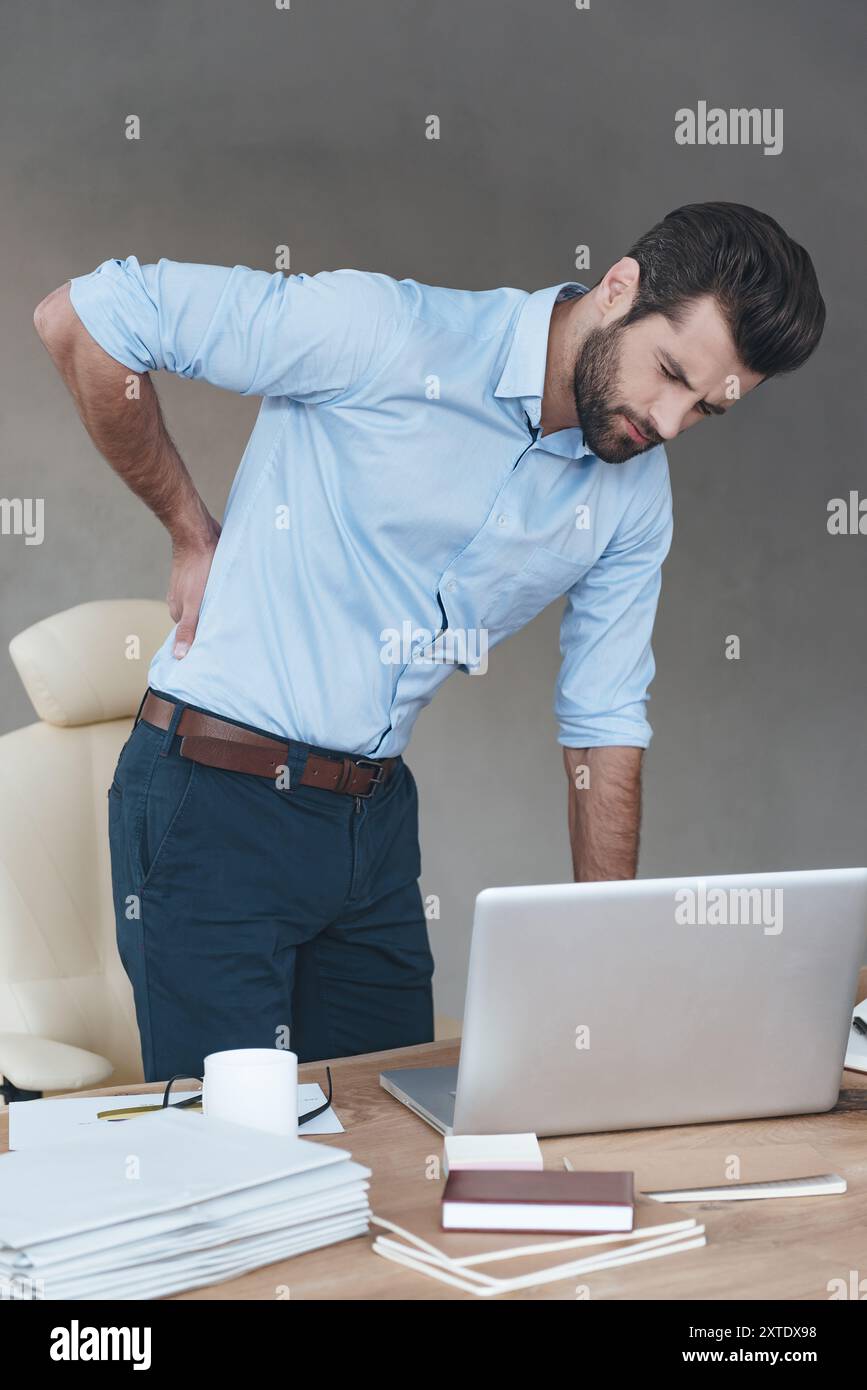 Back pain. Frustrated young handsome man looking exhausted while ...