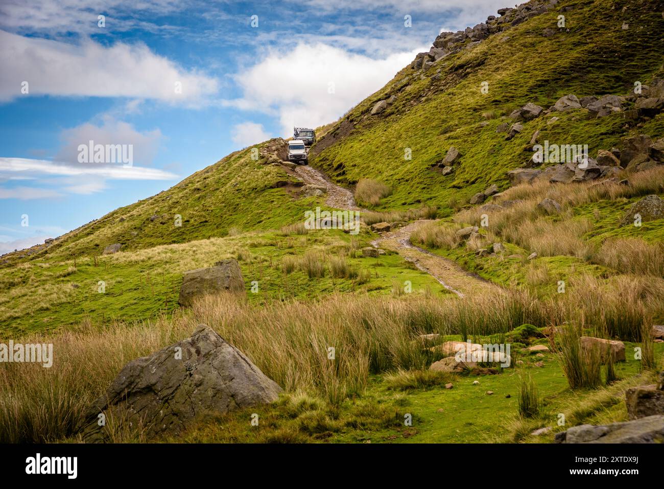 A small group of 4x4 vehicles descend a steep, grassy hill in the ...