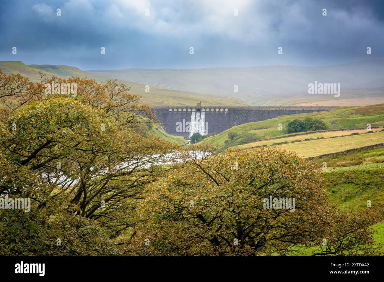 Water cascades over a Angram dam wall with autumnal trees in the ...