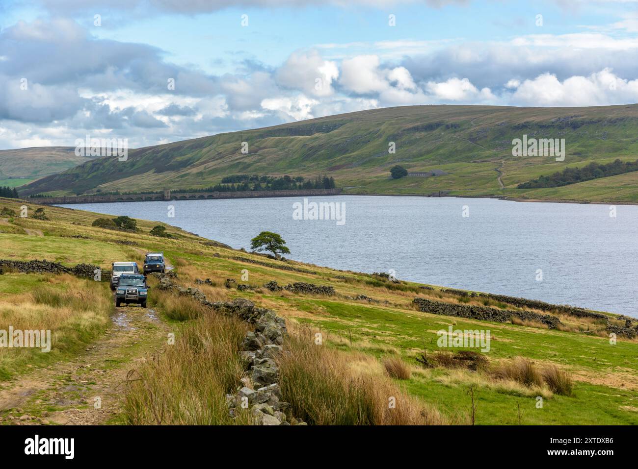 A small group of 4x4 vehicles navigate a rugged track along a tranquil ...