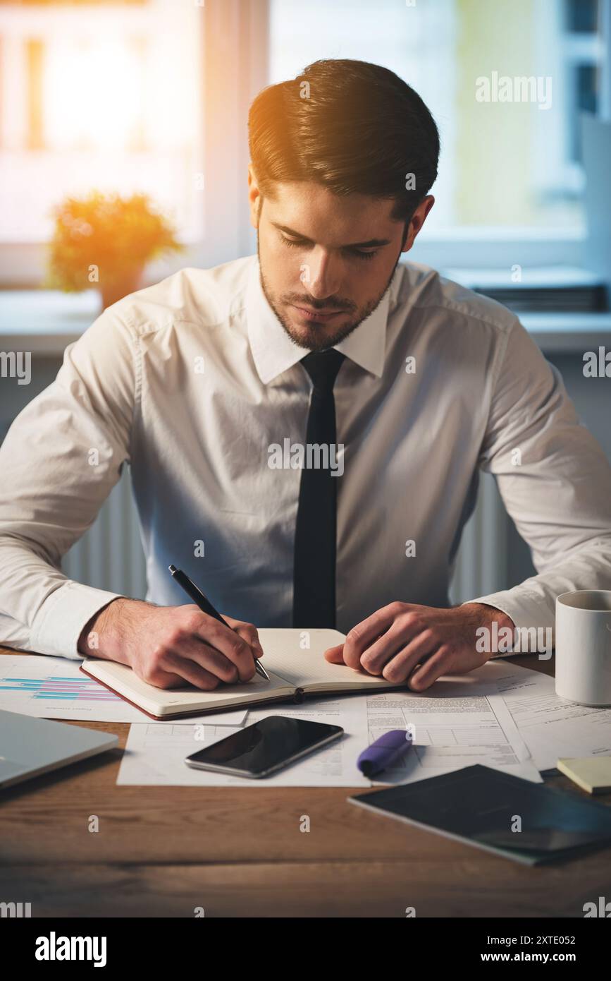 Making some notes. Pensive young handsome man writing in his notebook ...