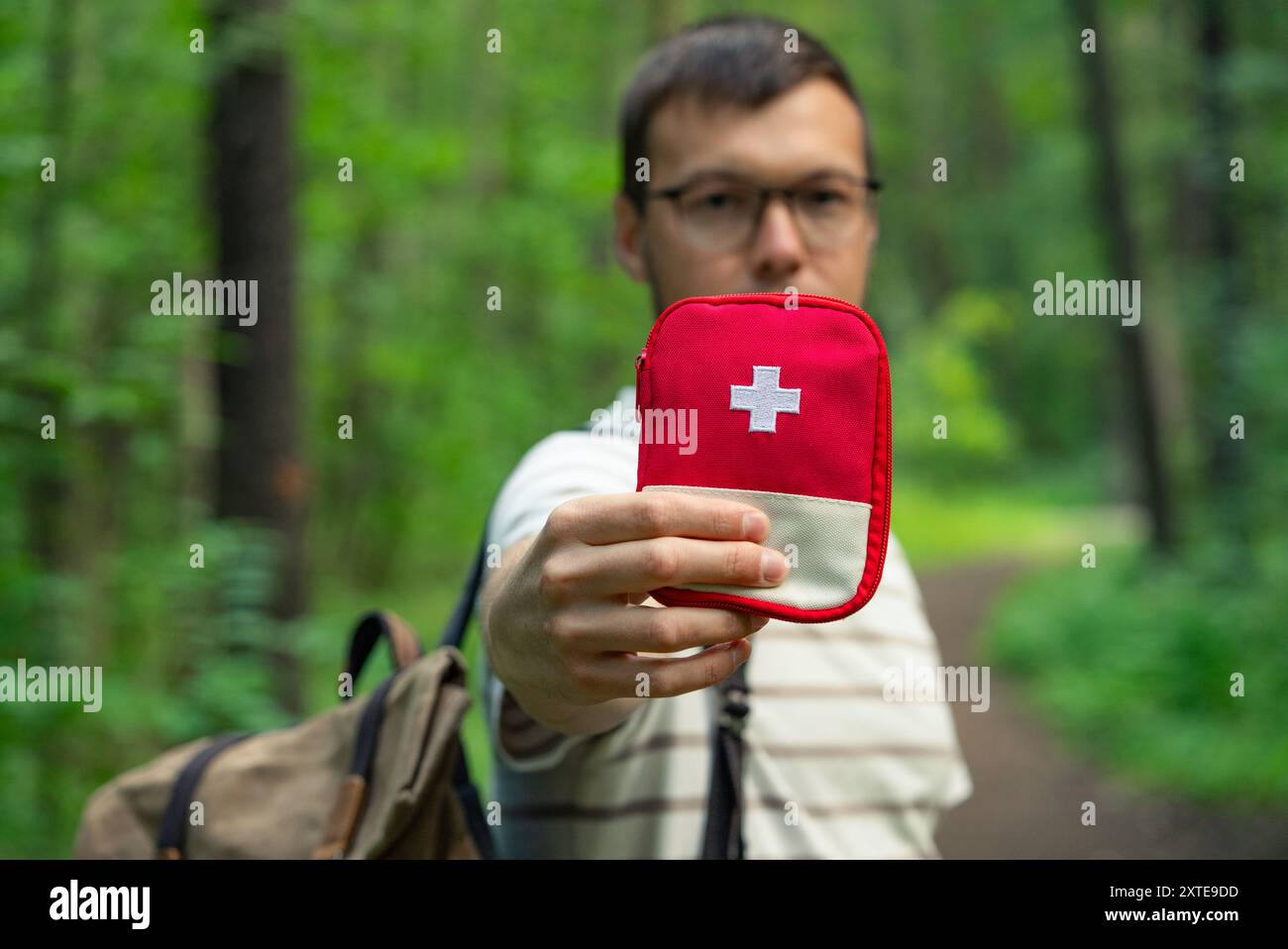 Hiker in the forest holds out a red first aid kit towards the camera ...