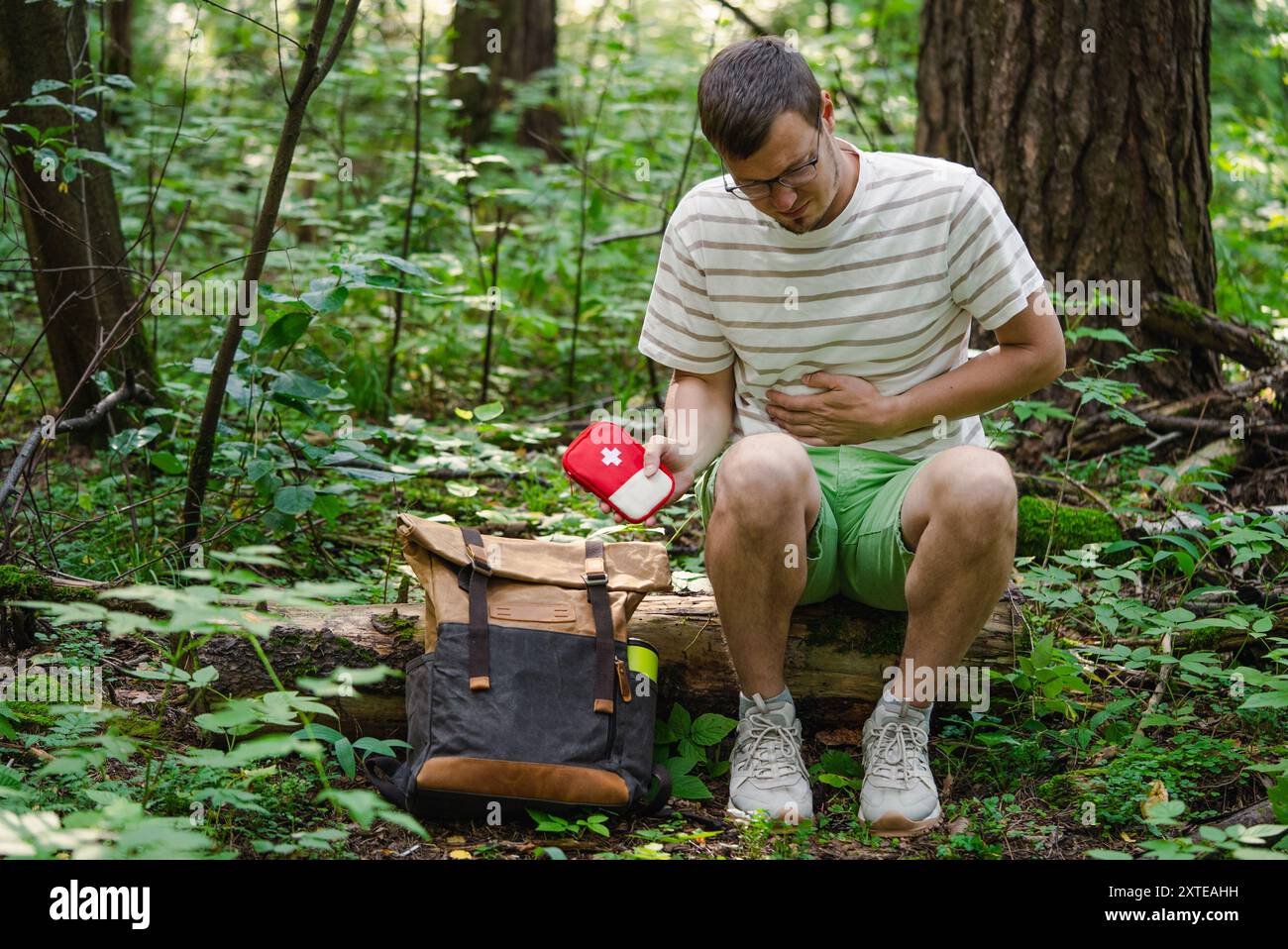 Man sitting on a log in a forest, holding his stomach in pain while ...