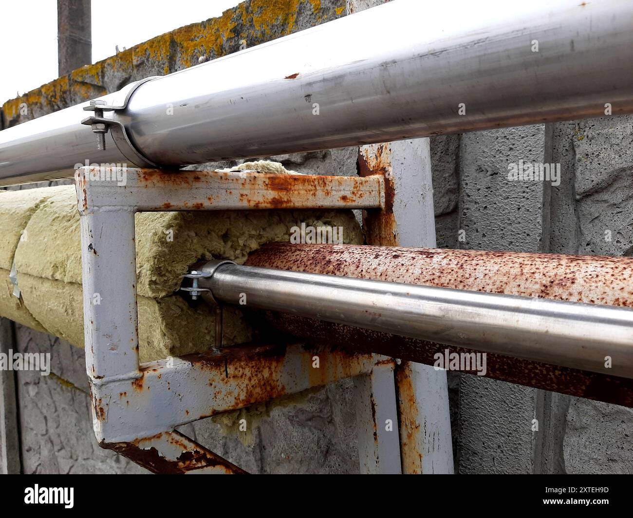 Metal pipes are mounted on a bracket, showcasing rust and insulation ...