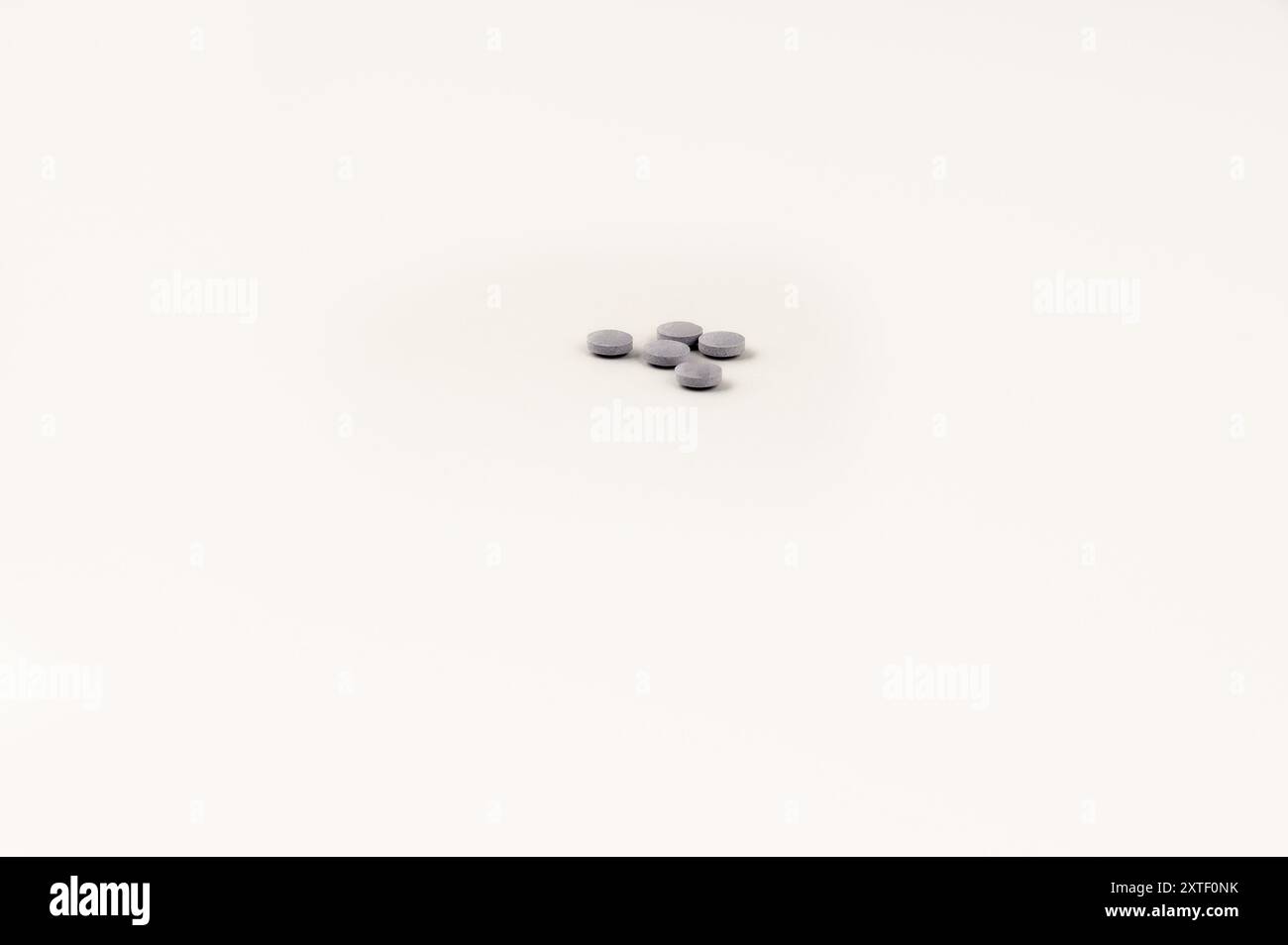Concept grouping of five small gray colored pills on white background ...