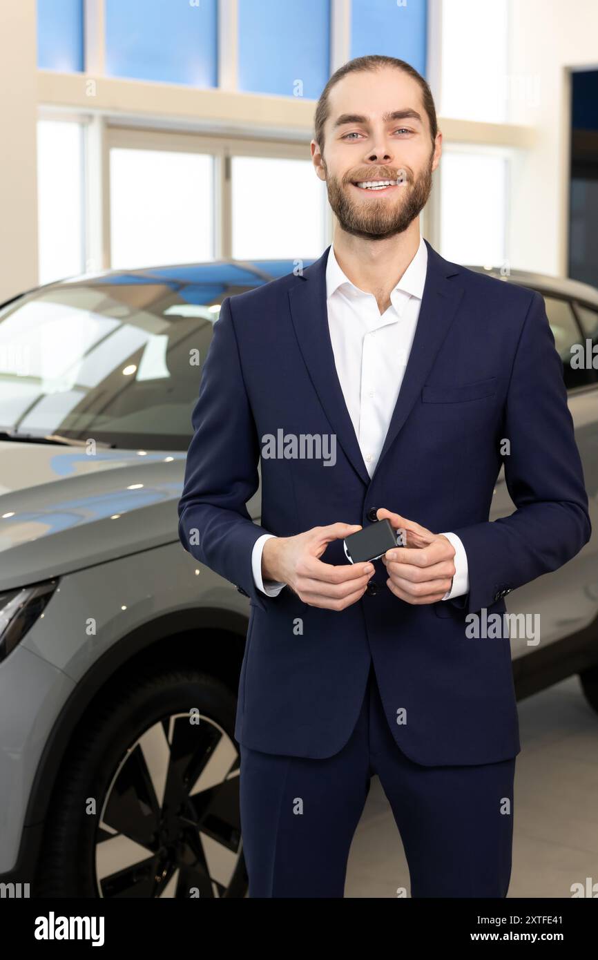 Man wearing suit standing in the car showroom with the vehicle indoors ...