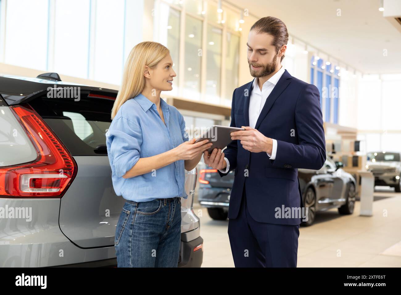 Stylish female potential buyer reviewing car with male agent at luxury ...