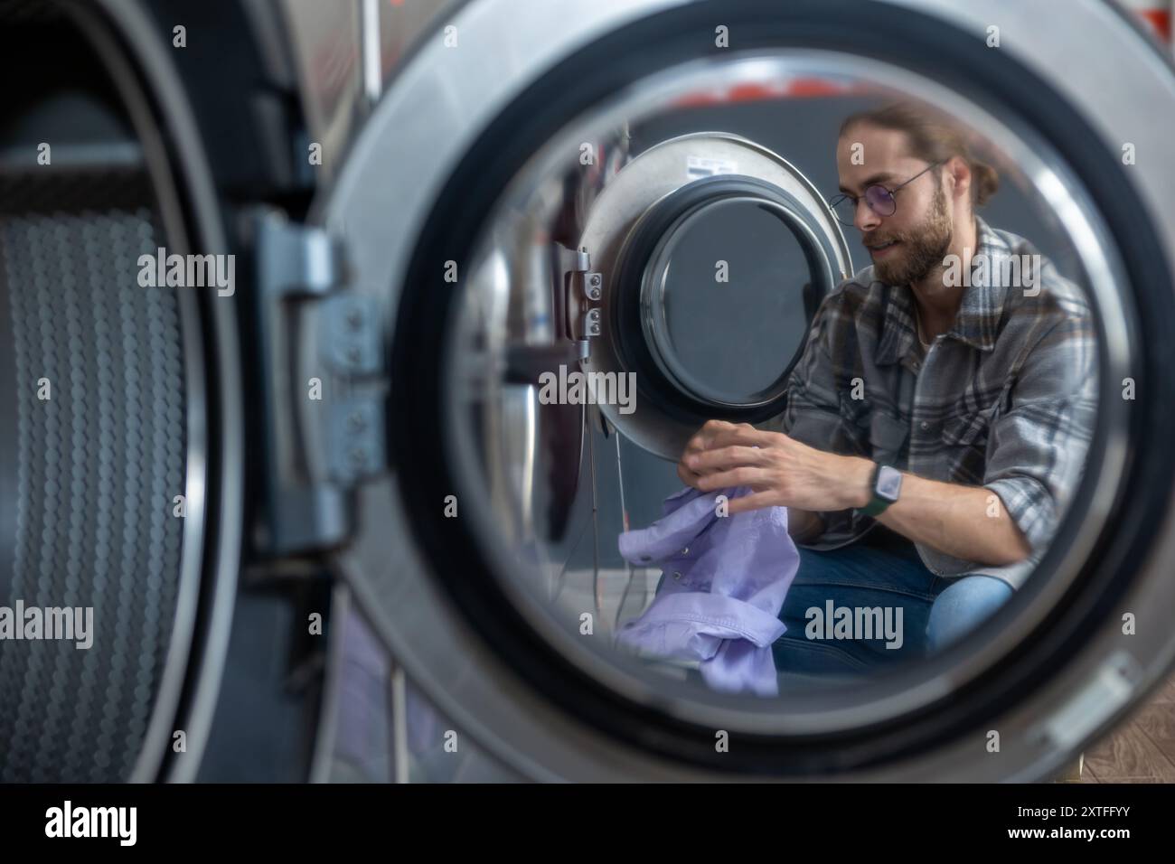 Hard working bearded man washing clothes at self-service laundromat ...