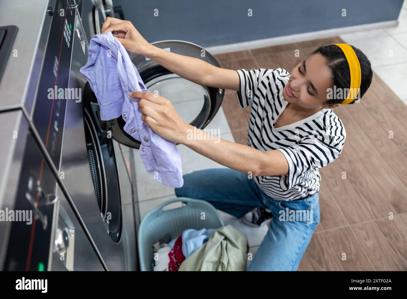 Woman in striped shirt doing routine laundry tasks at self-service laundromat Stock Photo - Alamy