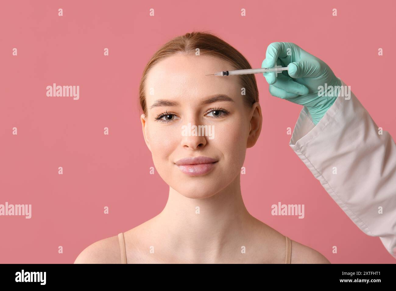 Beautiful young woman receiving filler injection in forehead on pink ...