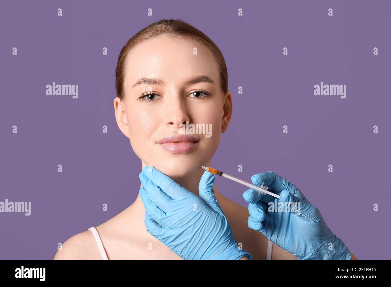 Beautiful young woman receiving filler injection in chin on purple ...