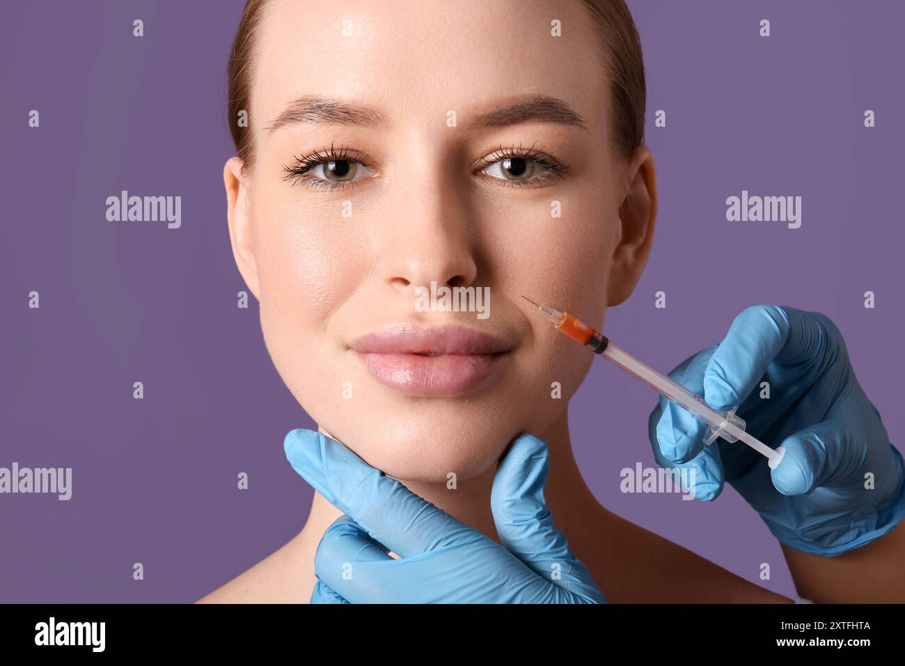 Beautiful young woman receiving filler injection in face on purple ...