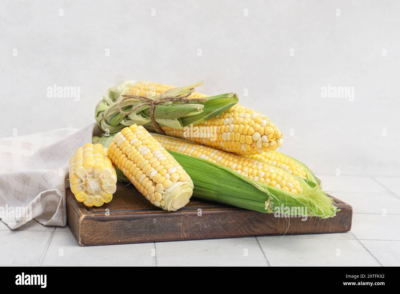 Wooden board with fresh corn cobs and napkin on white tile table Stock ...