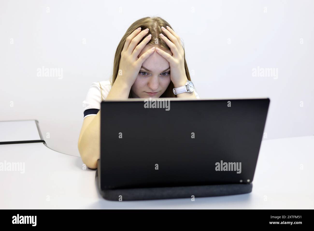 Girl with long hair sitting at office table with laptop clutching her head with her hands ...
