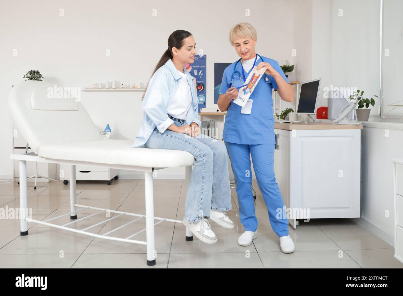 Female endocrinologist showing structure of thyroid gland to patient in ...