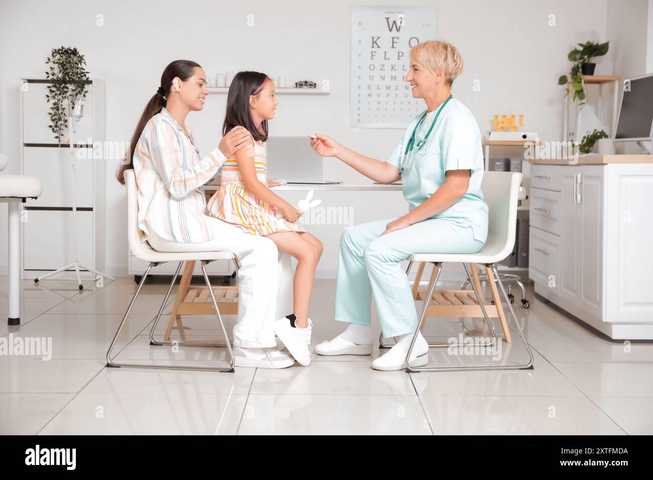 Female pediatrician giving thermometer to little girl and mother in ...