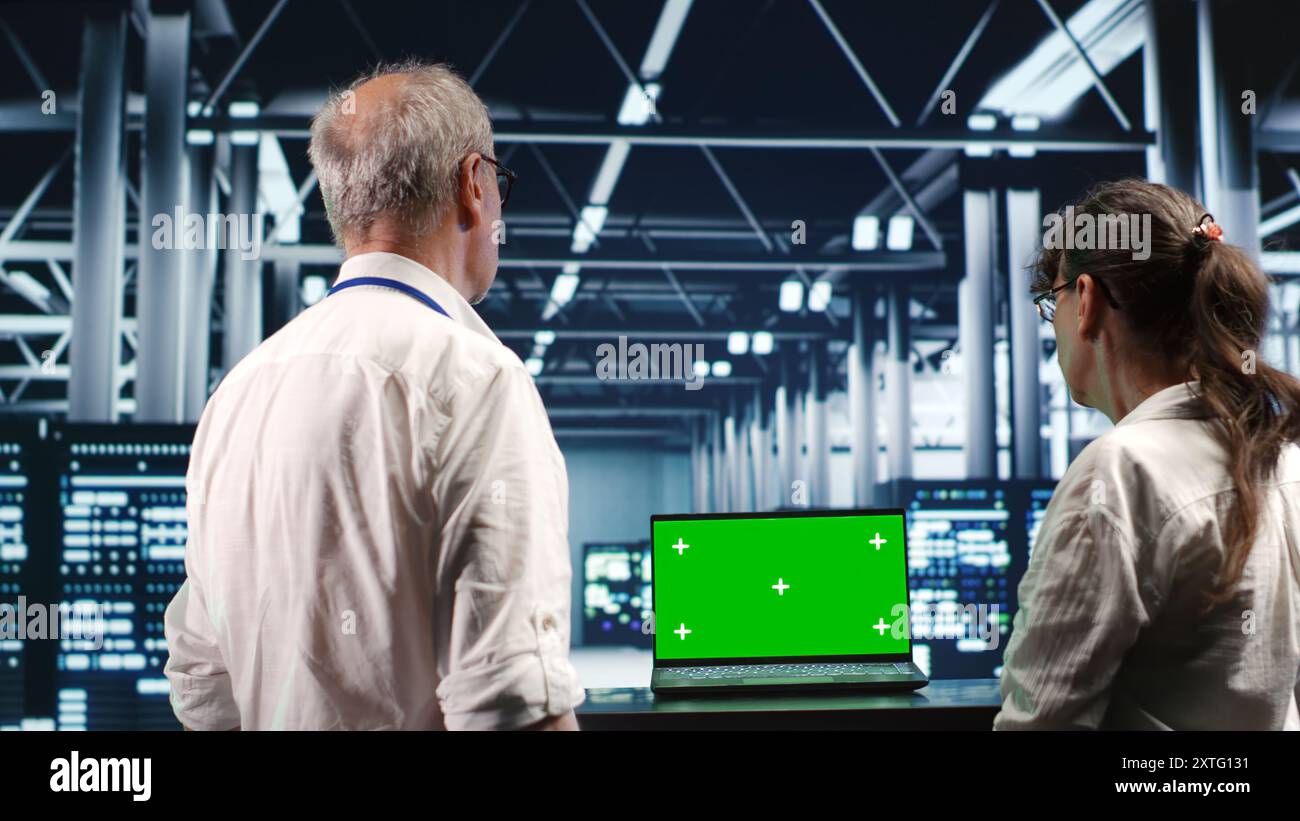 Certified IT programmers looking around high tech data center, using green screen laptop to ...