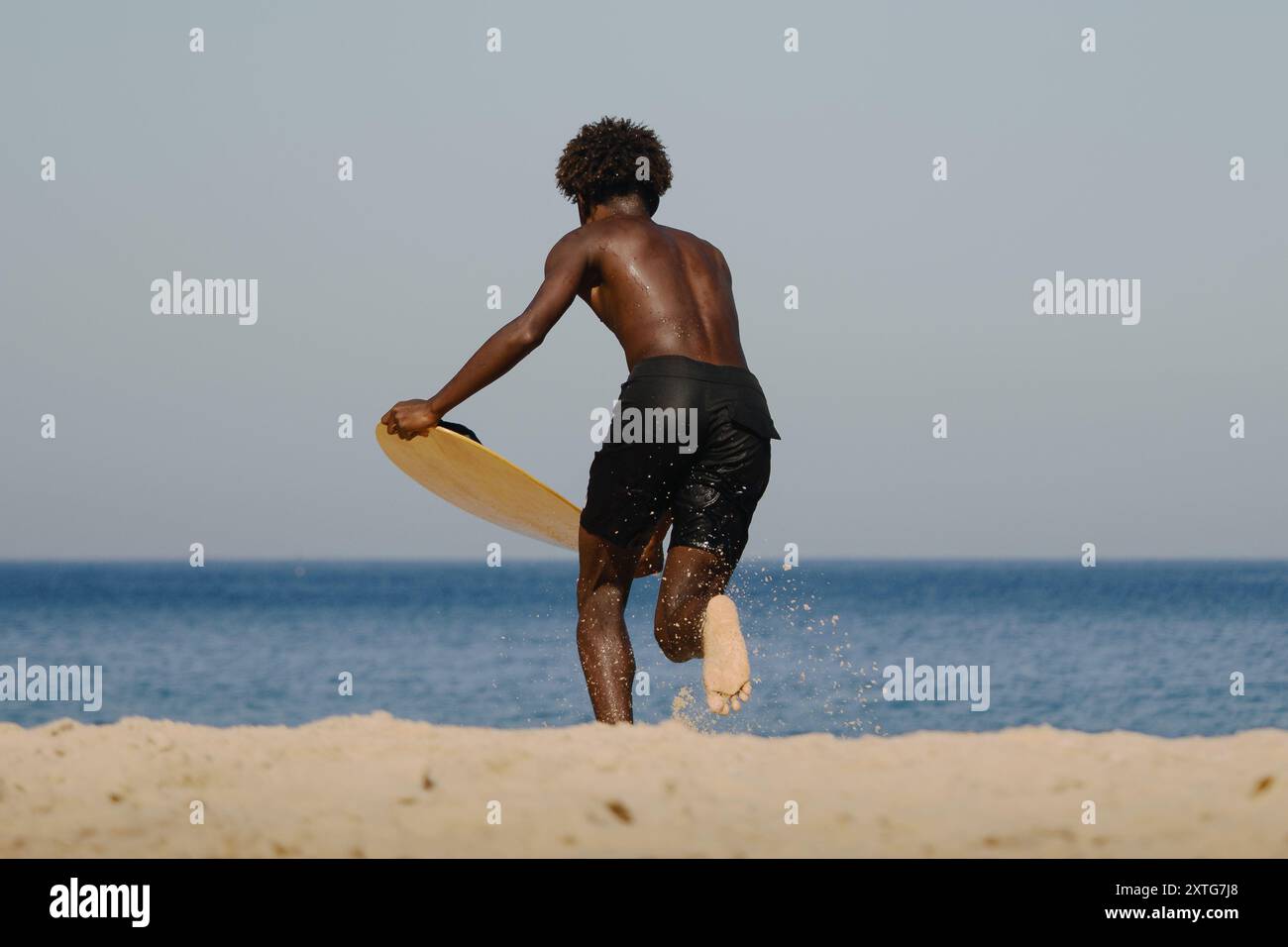 A young man running on the beach with a skimboard in hand, ready to ...