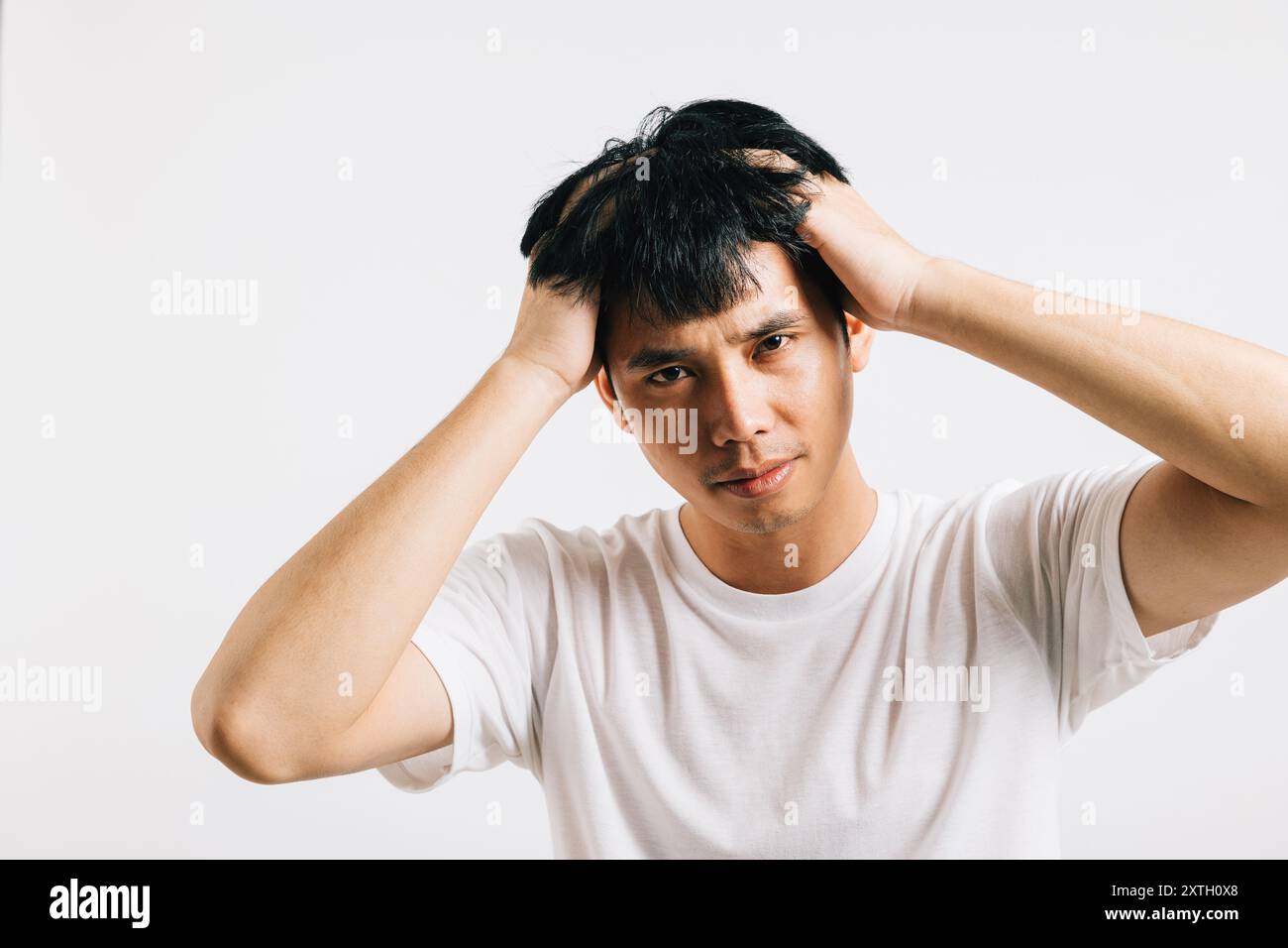 Asian man, battling stress and throbbing headache, holds head with a ...