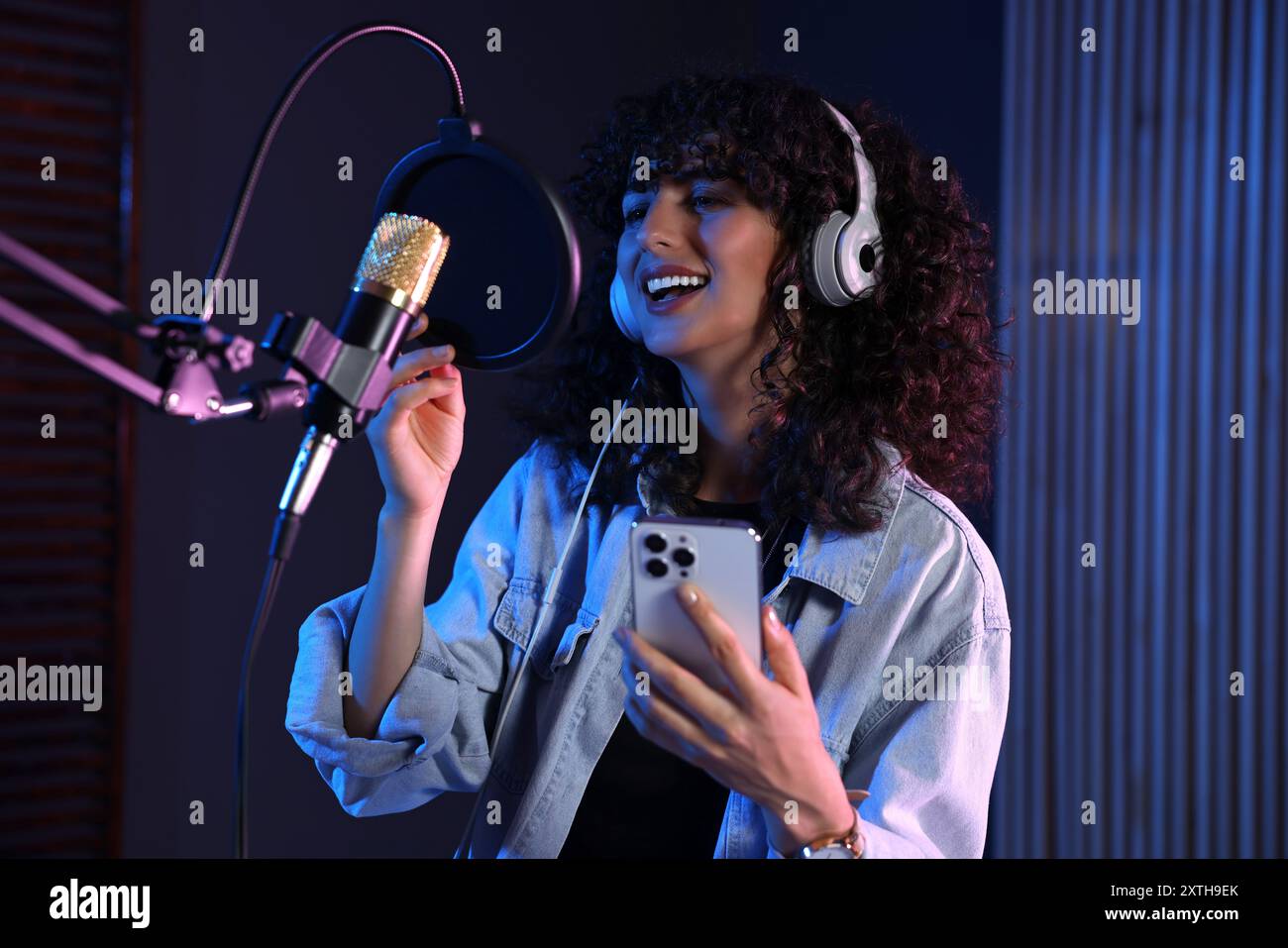 Vocalist with smartphone singing into microphone in professional record ...