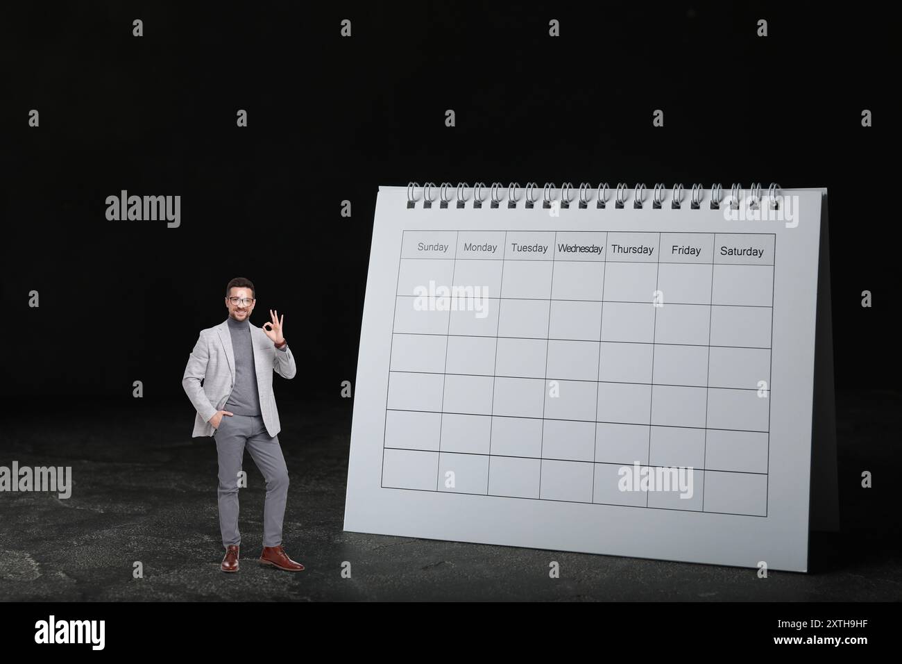 Happy small businessman showing Ok sign near big calendar on black ...