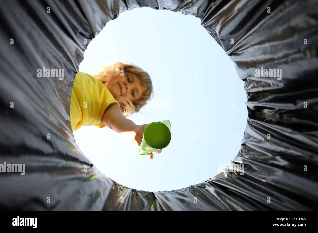Cute little girl throwing garbage into trash bin outdoors, bottom view ...