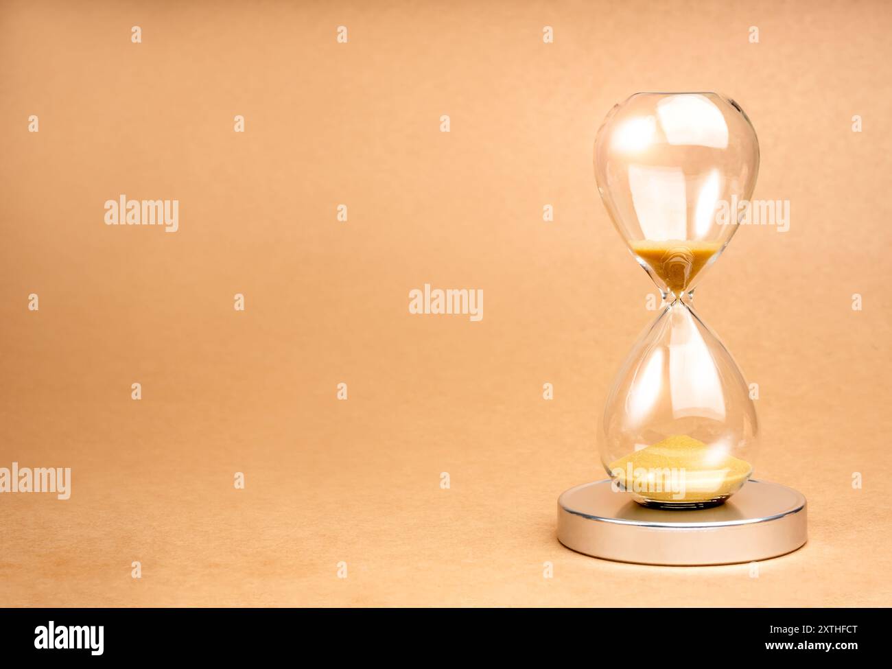 A clear hourglass with gold sand on chrome podium on light brown ...