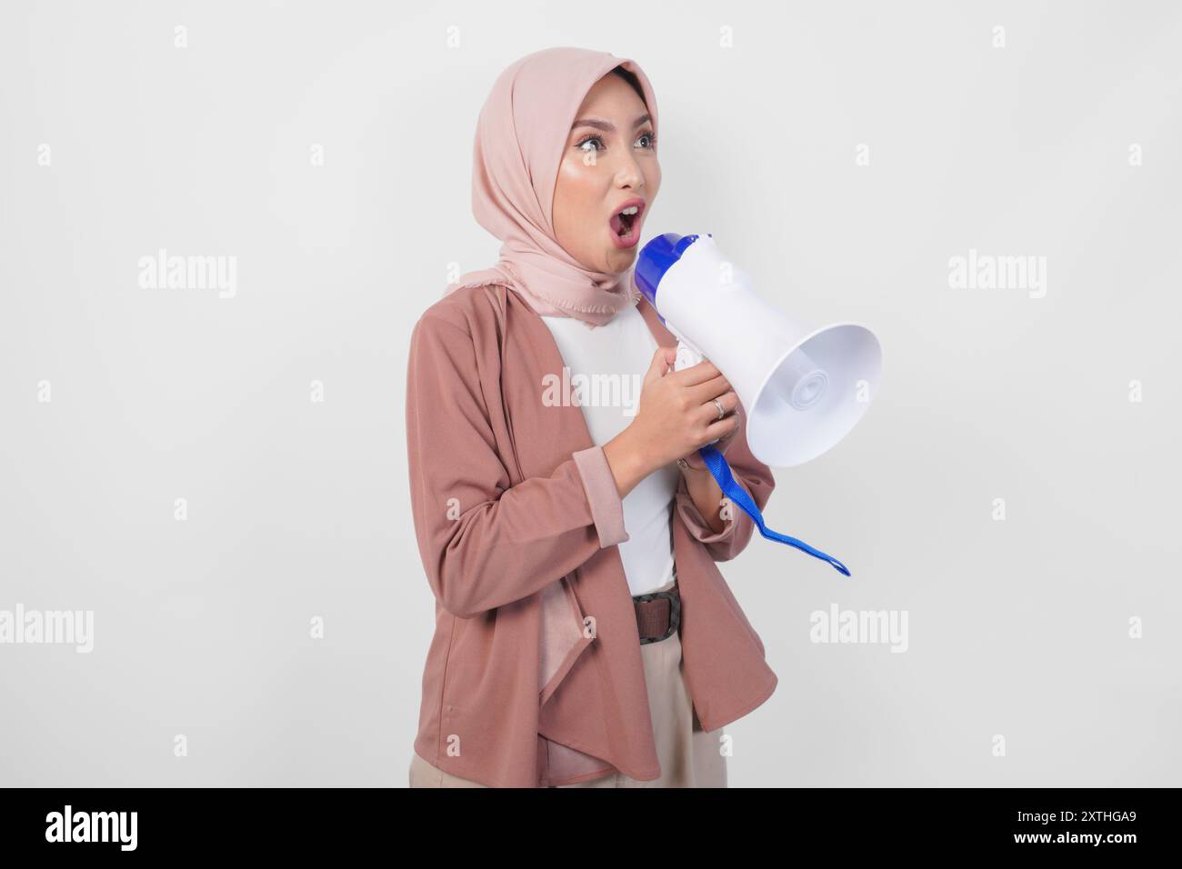 Lively young Asian muslim woman wearing hijab shouting at megaphone ...
