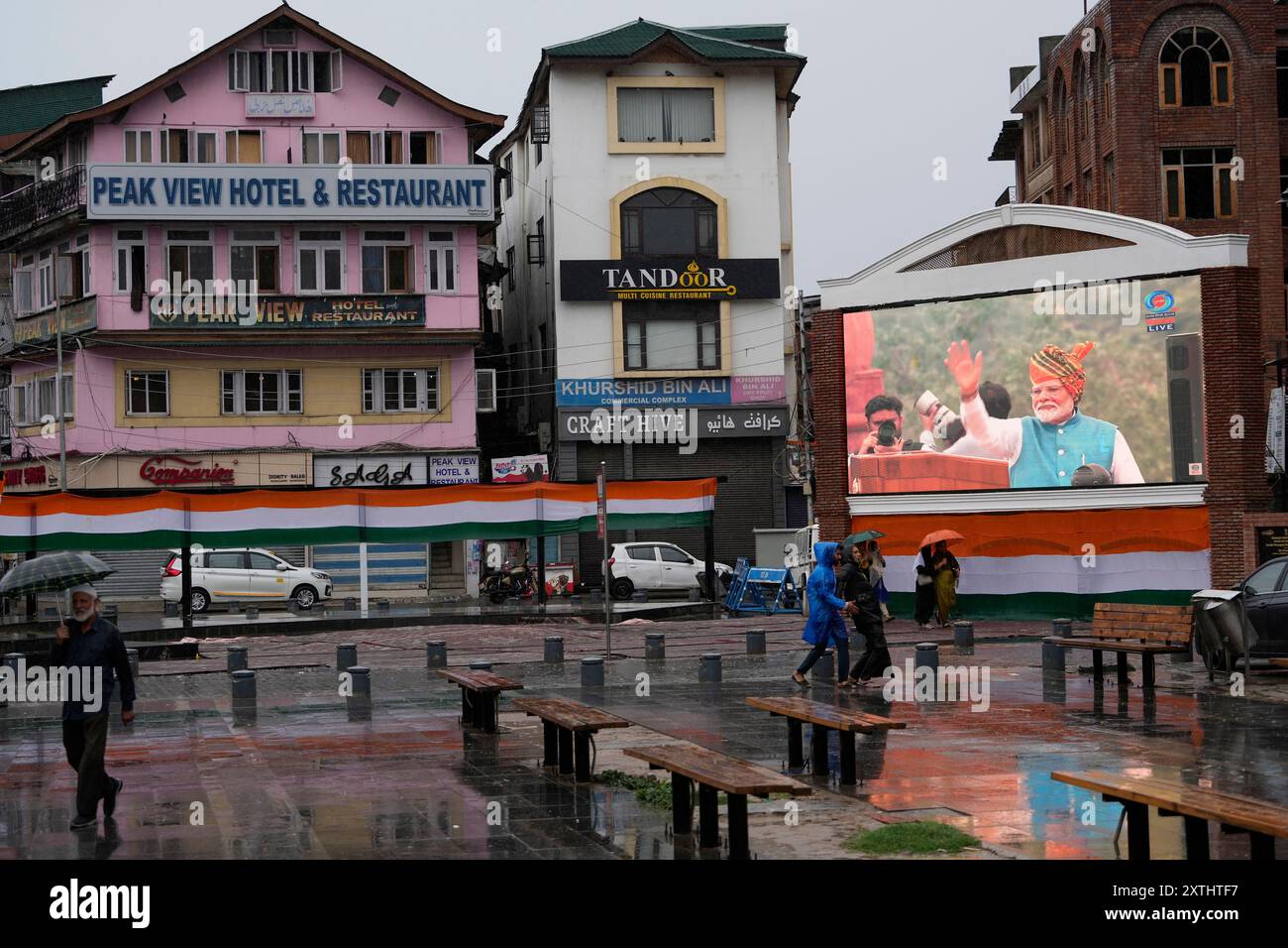 People walk in a rain as Indian Prime Minister Narendra Modi is seen on ...