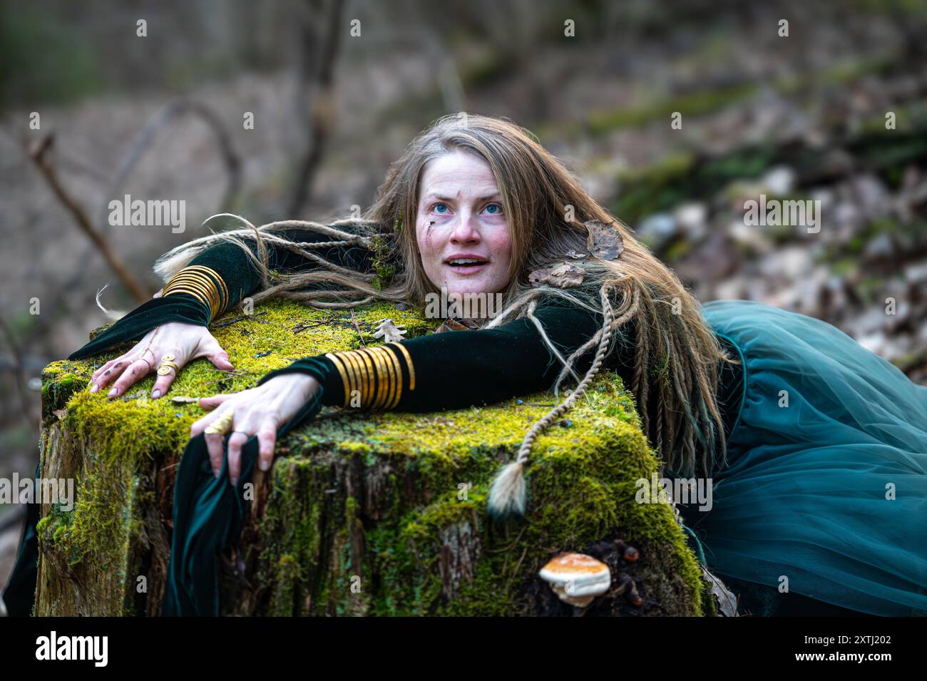 A woman leans on a moss-covered tree trunk in a forest. Shallow depth ...