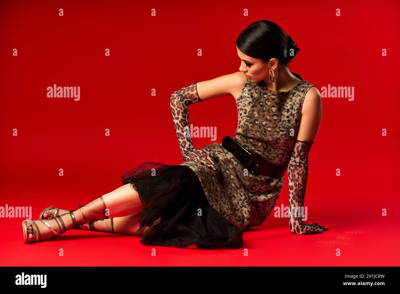 A young woman in a leopard print dress and gloves poses on a red ...