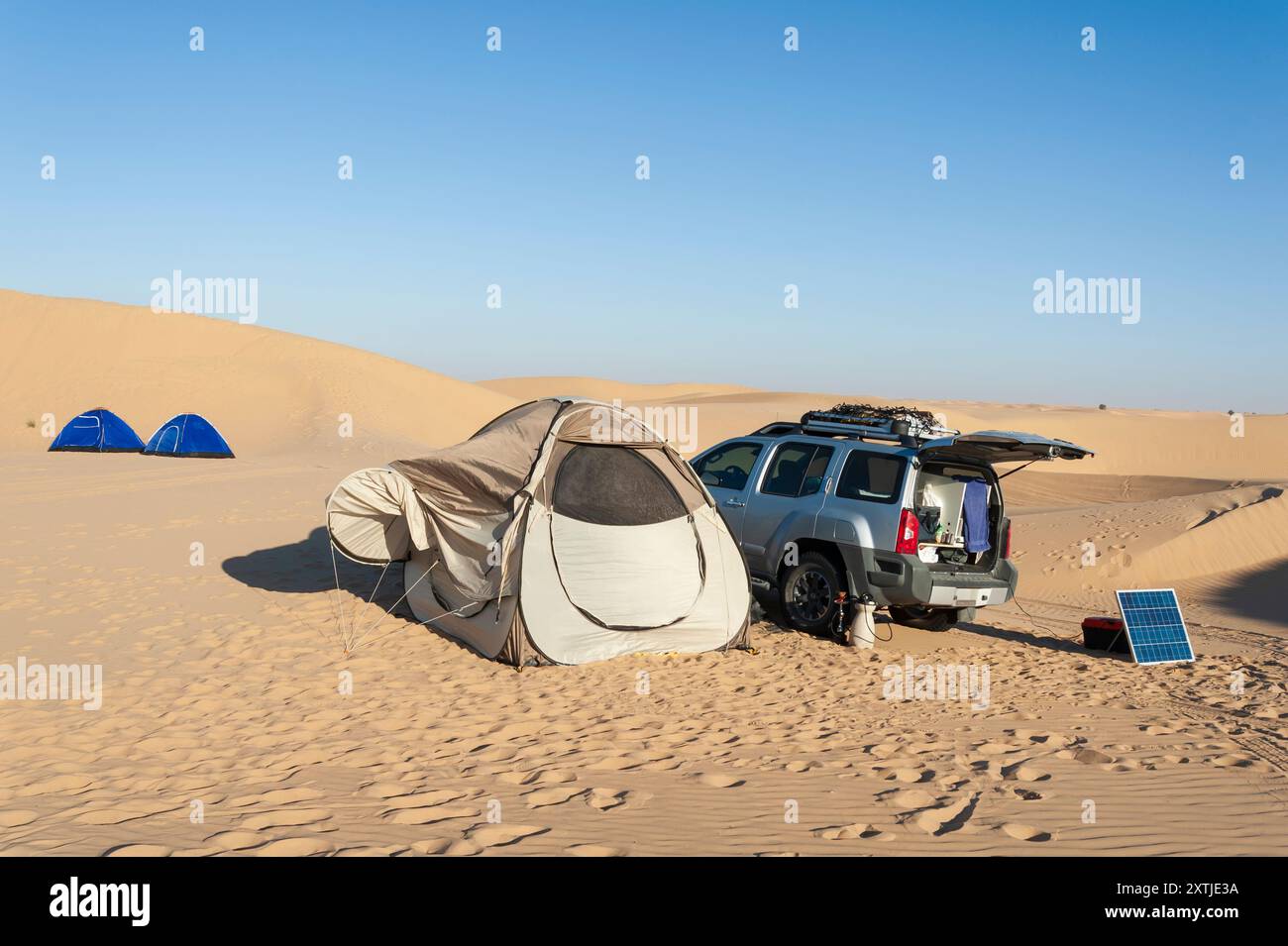 Off-road car, three tents, and solar panel setup in a vast desert ...