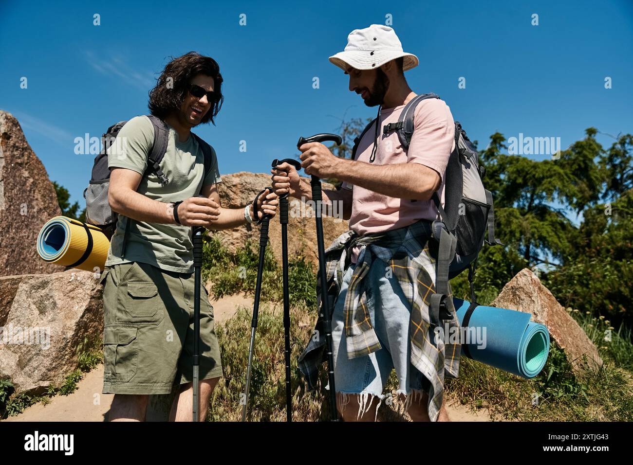 Two young men hike through a summer landscape, using trekking poles to ...