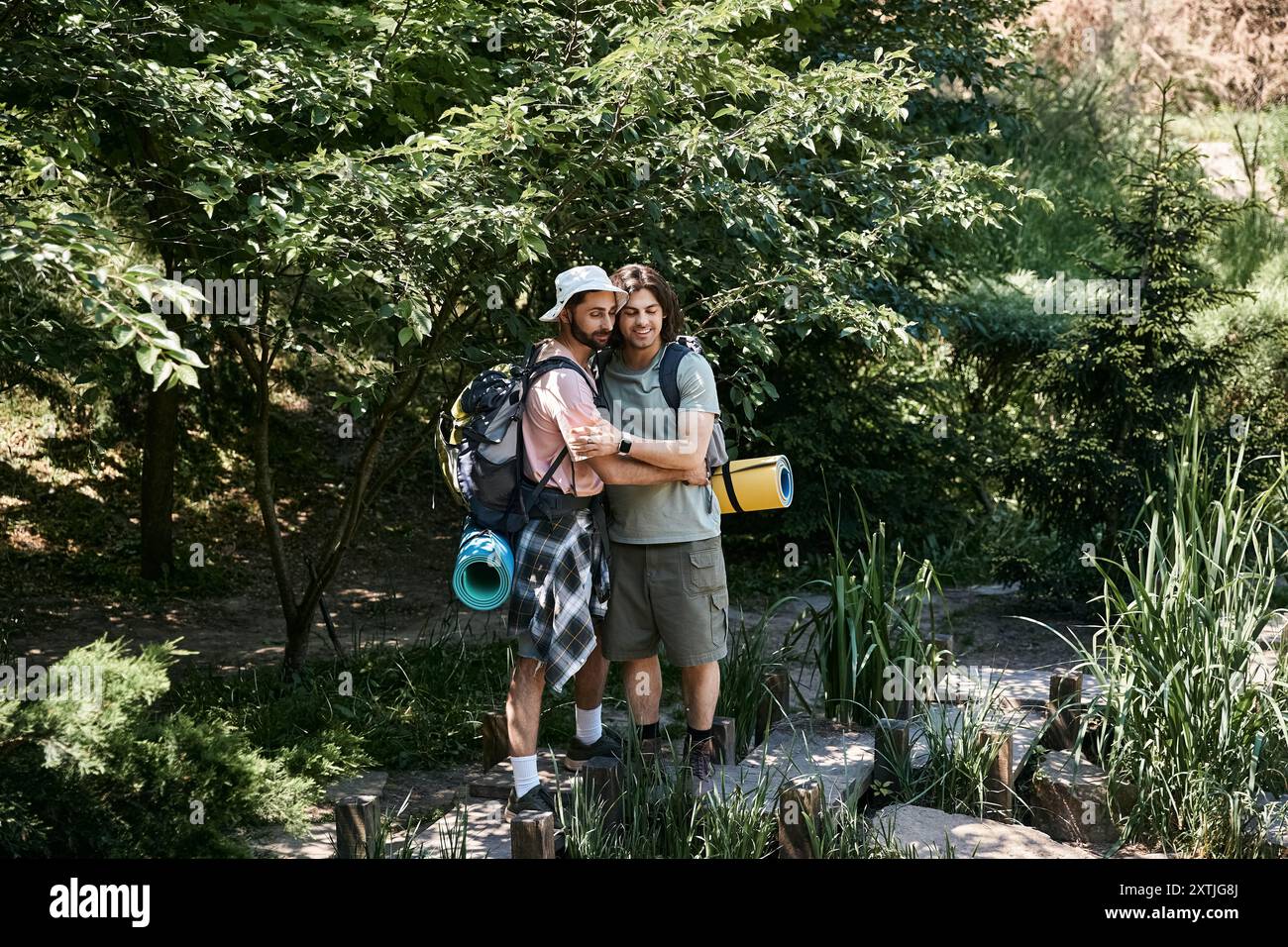 Two young men hike through a summer forest, embracing each other and ...