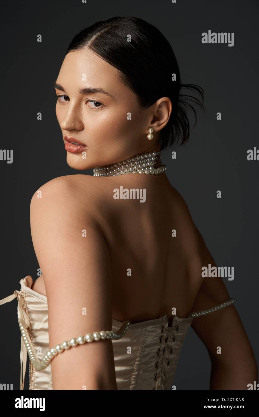A young woman with brunette hair and a pearl necklace poses against a dark background ...