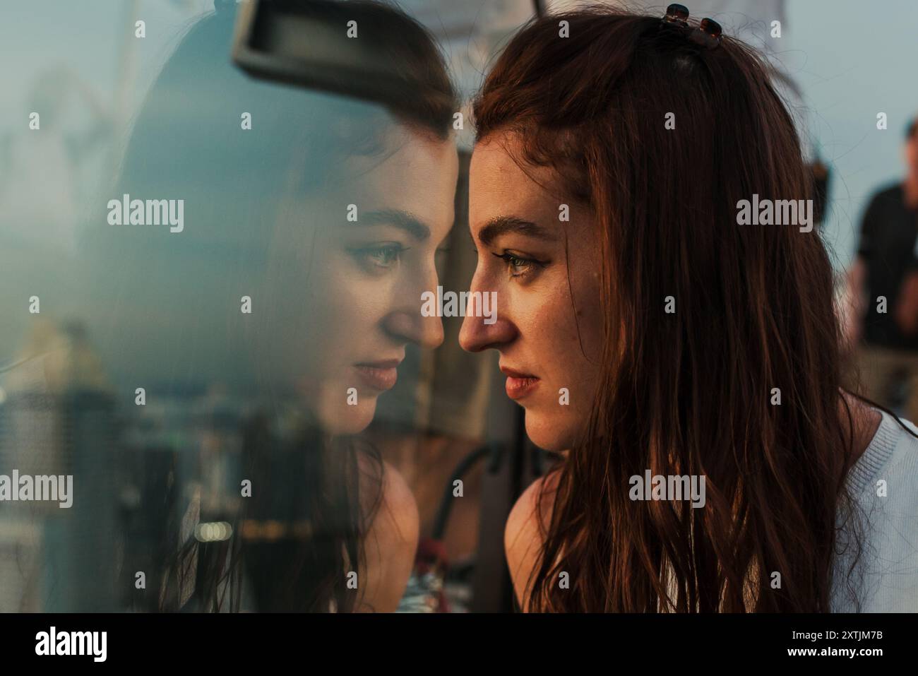 A young woman with long brown hair looks intensely at her reflection in ...